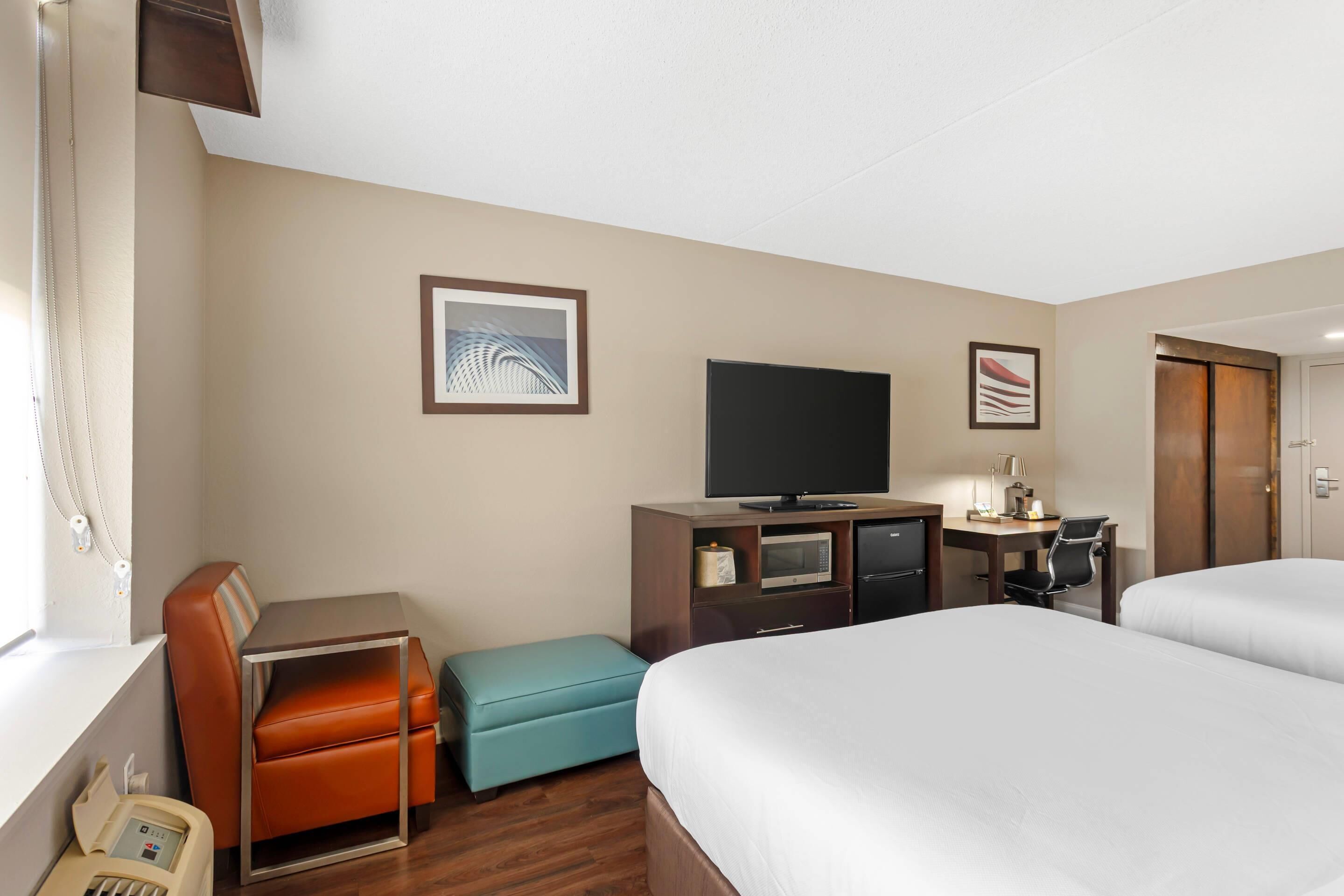 Quarto de hotel com cama, escrivaninha com televisão, um cantinho de estar e micro-ondas.
