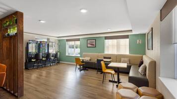 Uma área de lounge moderna com divisória de madeira, máquinas de jogos e disposição de assentos incluindo um sofá e cadeiras.