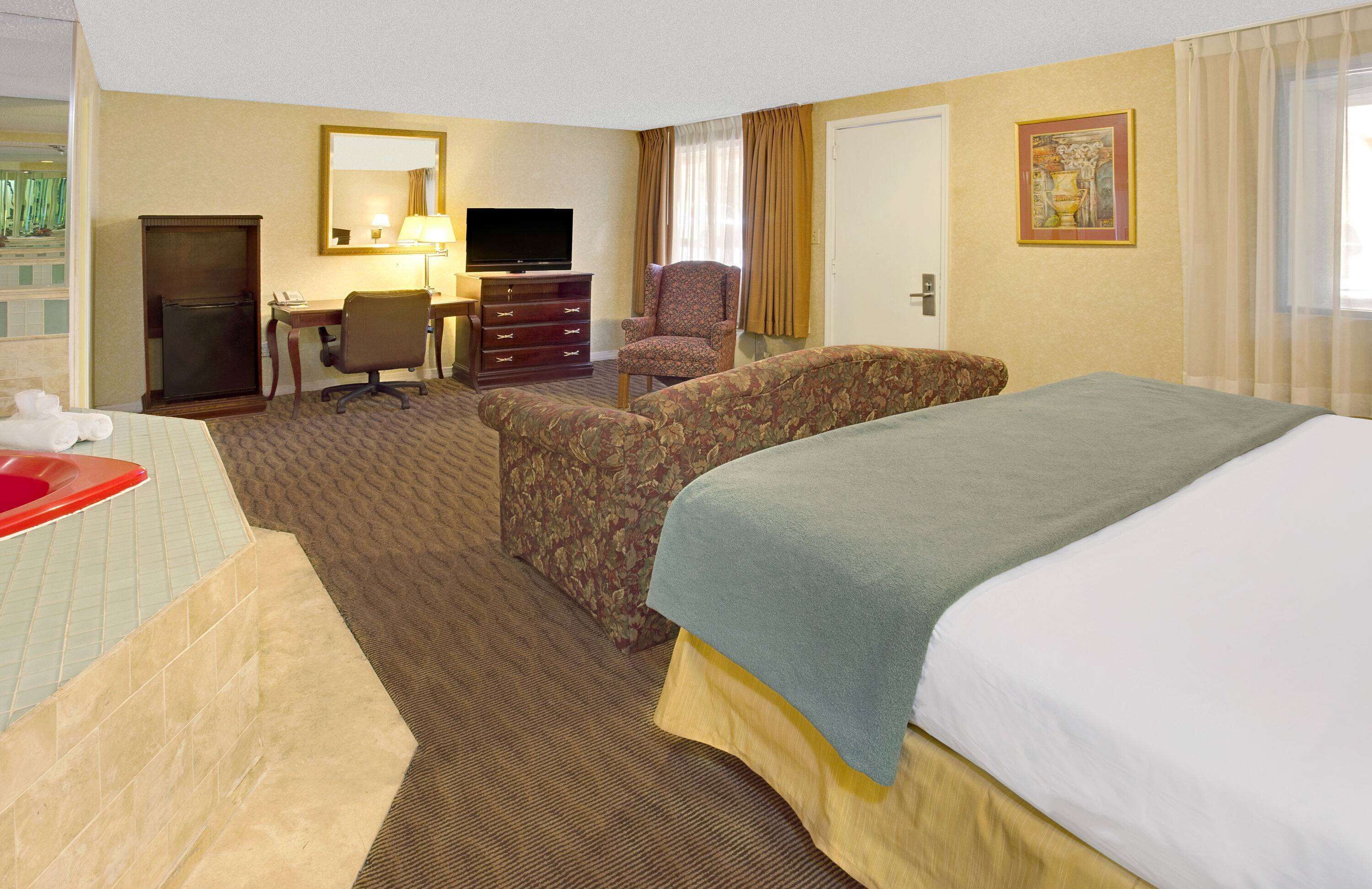 Quarto de hotel com cama, escrivaninha com computador, cadeira, televisão e lareira.