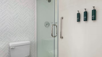 Um banheiro com box de vidro, vaso sanitário e três garrafas verdes na parede.