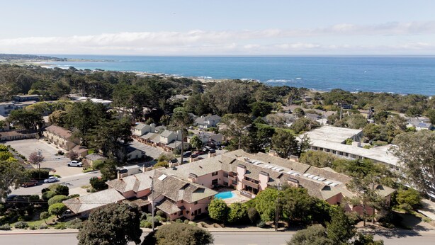Zona residencial com um edifício grande, piscina, árvores e vista para o oceano.