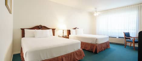Quarto de hotel com duas camas, uma escrivaninha, uma cadeira e uma janela com cortinas.