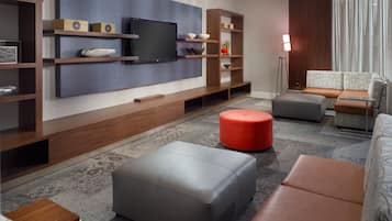 Uma sala de estar moderna com uma TV de tela plana, prateleiras de madeira, pufes e um sofá estampado.
