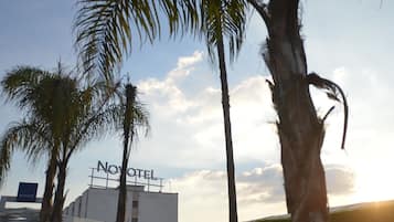 Um hotel Novotel com vista clara para o céu e palmeiras em primeiro plano.
