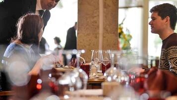 Um restaurante com uma mesa posta para dois, copos e um garçom atendendo os hóspedes.