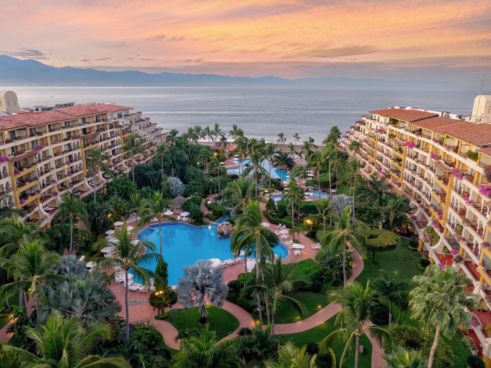 Um resort com várias varandas, piscina central e vista para o mar.