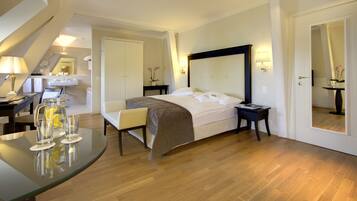 Quarto de hotel com cama, mesas de cabeceira, escrivaninha com abajur, uma cadeira e uma mesa de vidro com jarra e copos.