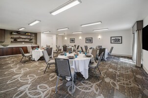 Sala de conferências com mesas redondas, cadeiras e uma área de buffet.