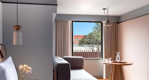 Quarto de hotel moderno com sofá, uma mesinha com um vaso e um livro, e uma janela com cortinas.