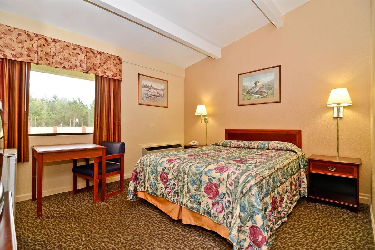 Quarto de hotel com cama, escrivaninha, cadeira, duas luminárias na parede e duas imagens emolduradas.