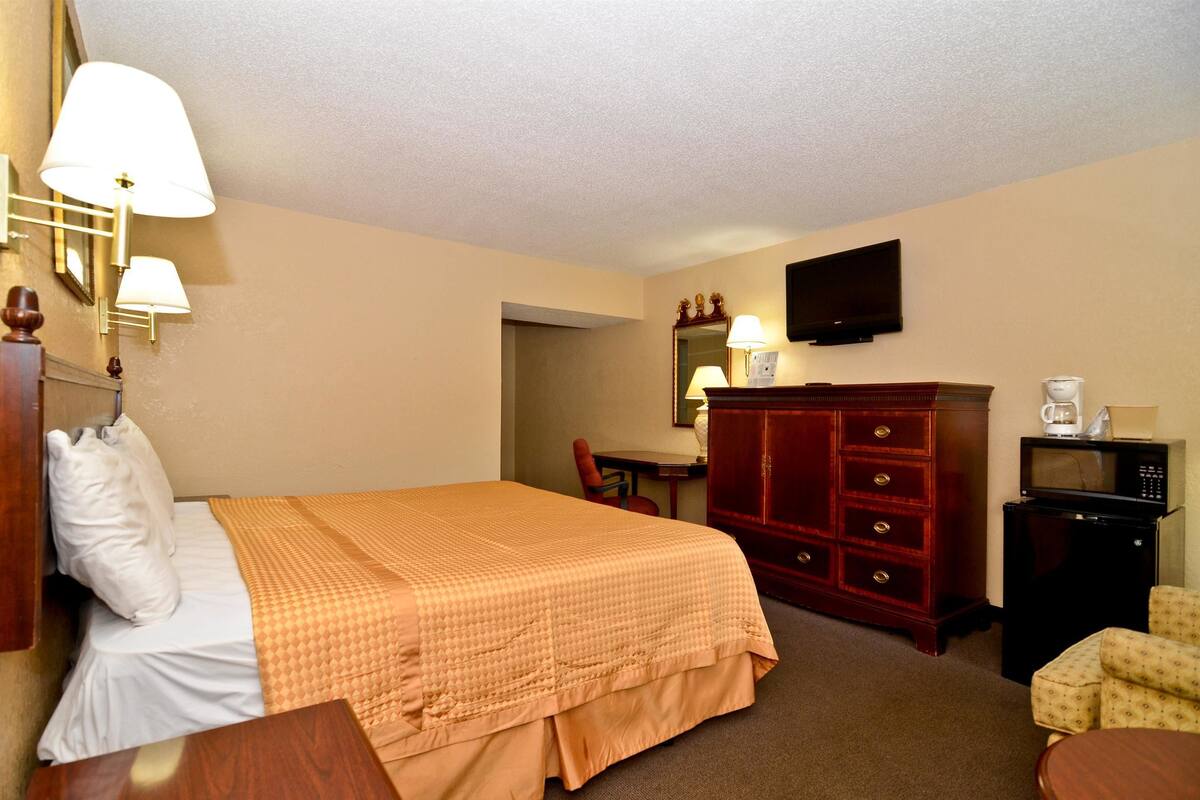 Quarto de hotel com cama, escrivaninha, penteadeira, televisão e micro-ondas.