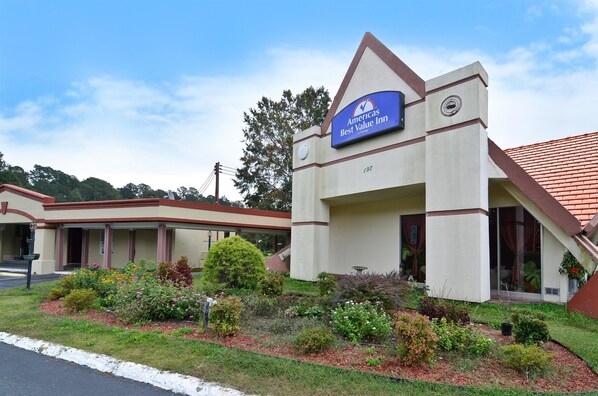 Um hotel com uma placa indicando "Americas Best Value Inn". Apresenta um design moderno, uma entrada destacada e um jardim paisagístico na frente.
