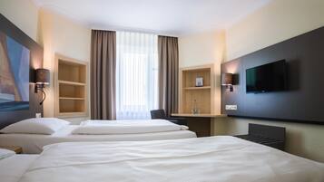 Quarto de hotel com duas camas, uma escrivaninha, uma cadeira, uma televisão e uma janela com cortinas.