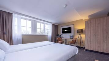Quarto de hotel com duas camas, uma escrivaninha, uma cadeira, uma televisão e um guarda-roupa.