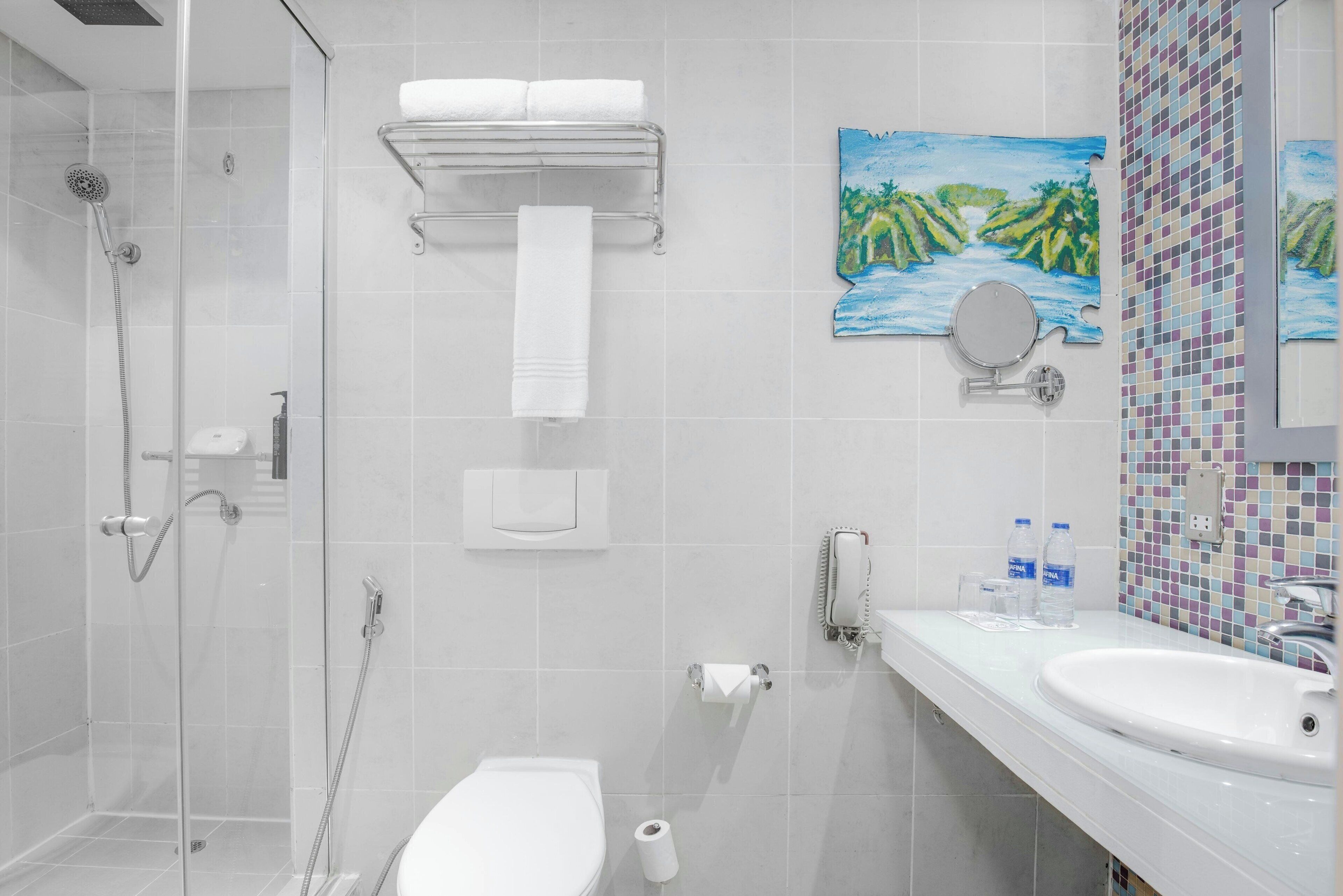 Uma casa de banho moderna com cabine de chuveiro em vidro, sanita, lavatório com espelho e um porta-toalhas.