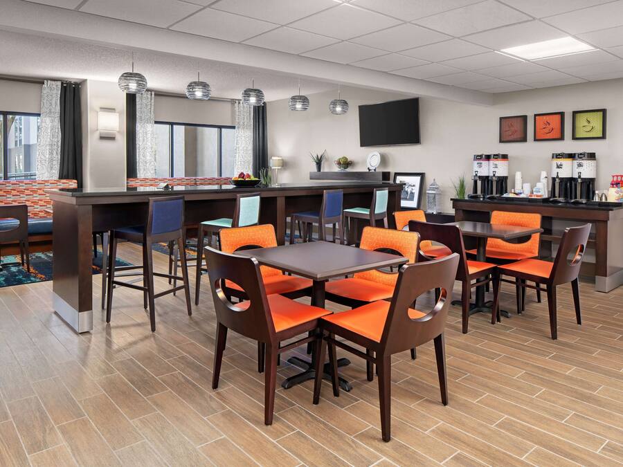 Uma área de refeições moderna com cadeiras e mesas laranja, um balcão de bar e uma televisão de tela plana na parede.