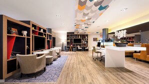 Um interior moderno com piso de madeira, área de estar central com cadeiras, uma mesa branca e uma TV sobre um móvel.