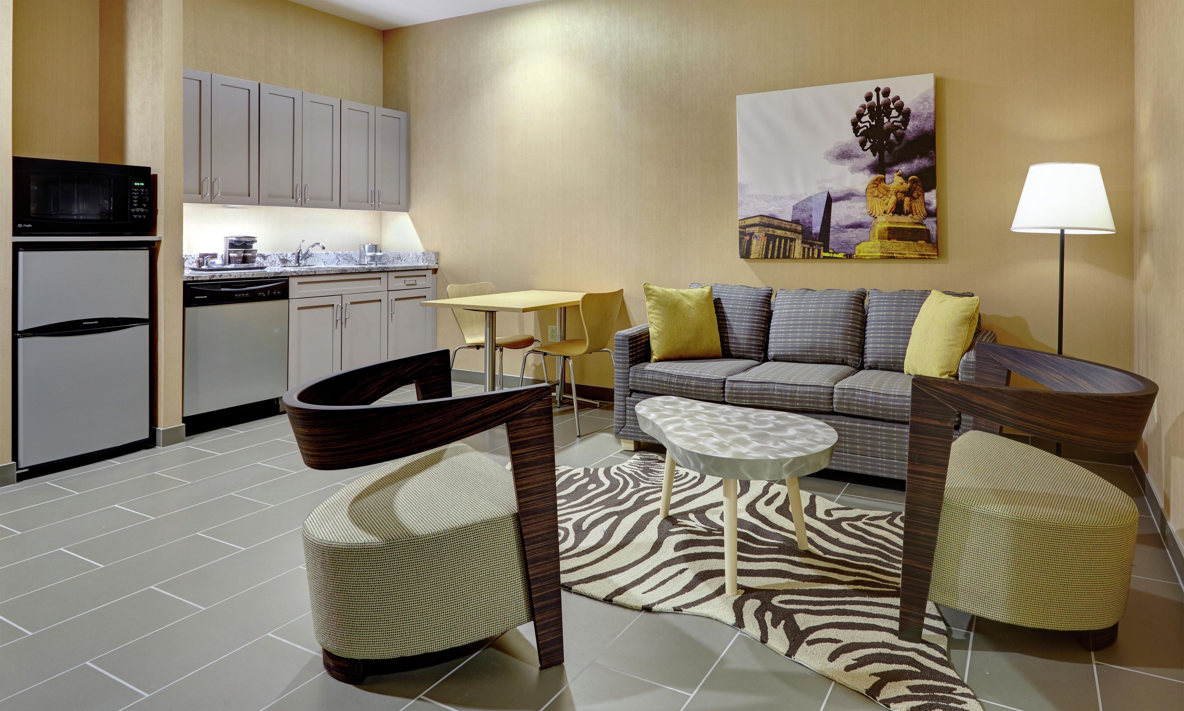 Espaço de estar compacto com cozinha compacta, sofá, mesa de jantar e tapete estampado com padrão de zebra.