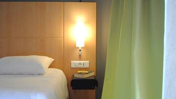 Quarto de hotel com uma cama, mesa de cabeceira com abajur, um livro e uma tomada.