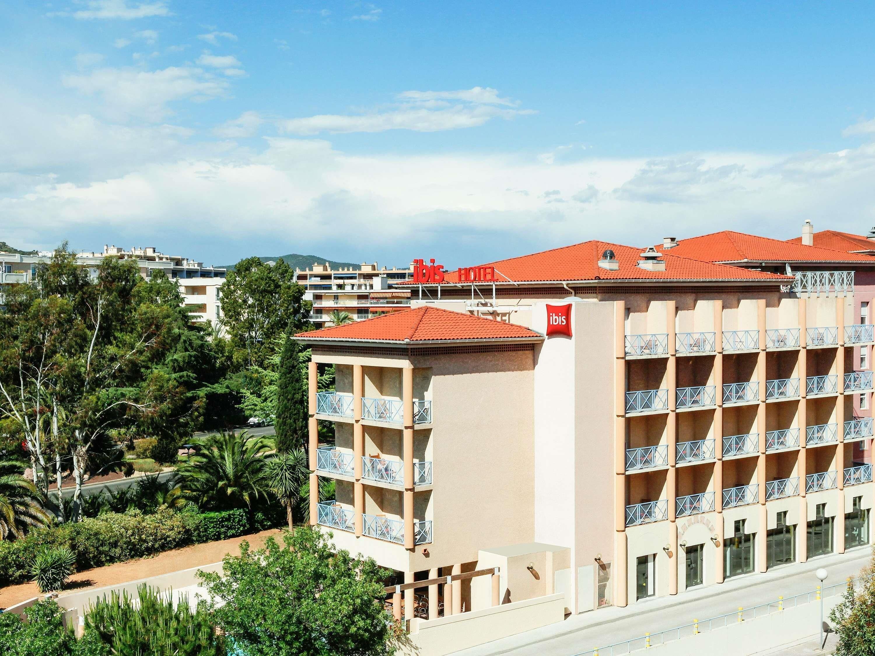 Um hotel com várias varandas, telhado vermelho e vista para edifícios e vegetação ao redor.