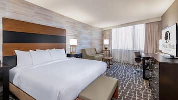 Quarto de hotel com uma cama grande, uma escrivaninha, uma cadeira e uma televisão.