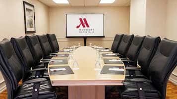 Uma sala de conferência com uma mesa comprida, cadeiras de couro preto e uma tela exibindo o logotipo da Marriott.