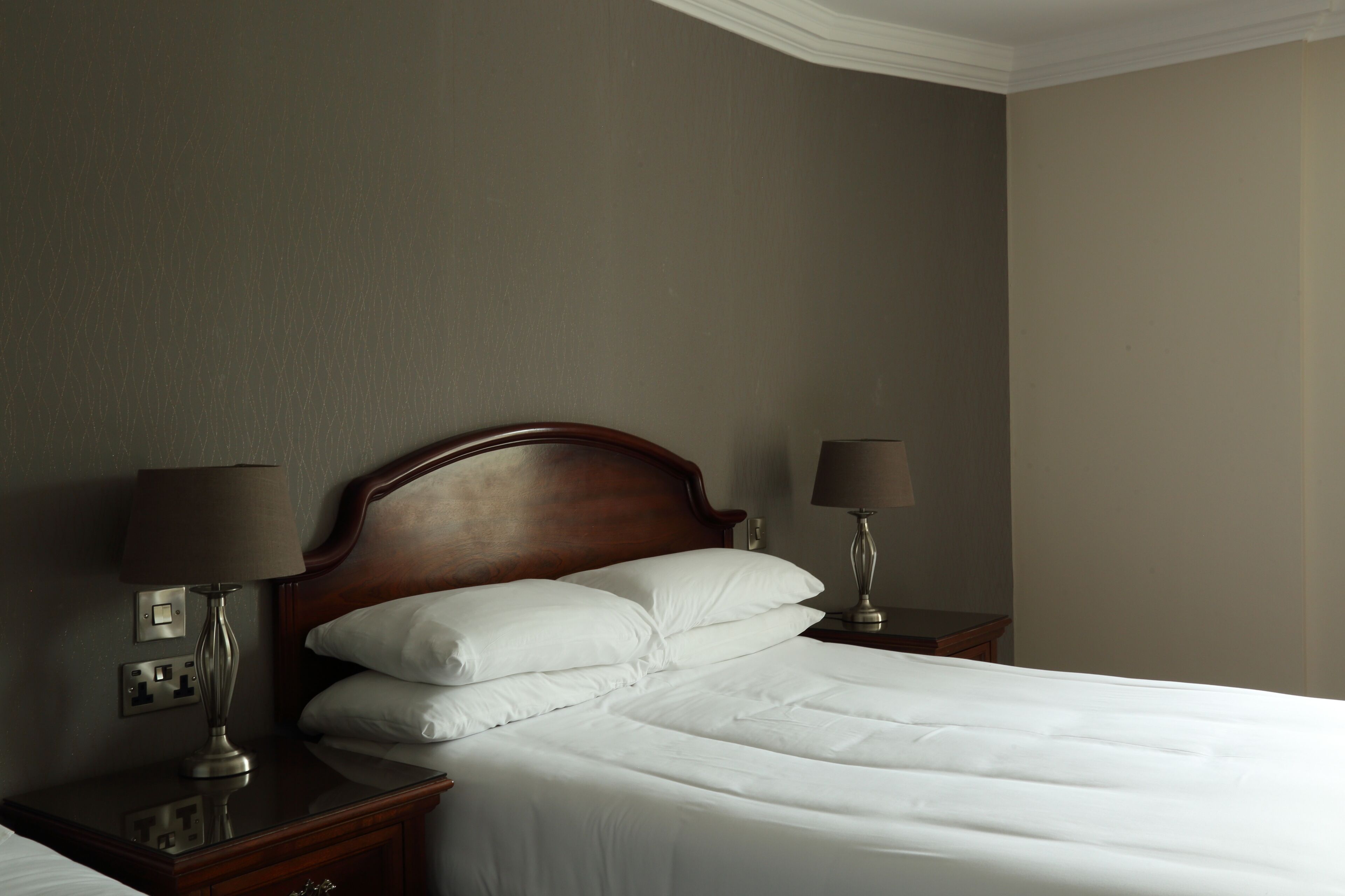 Cama bem arrumada com lençóis brancos, duas luminárias de cabeceira e uma cabeceira de madeira em quarto de hotel.