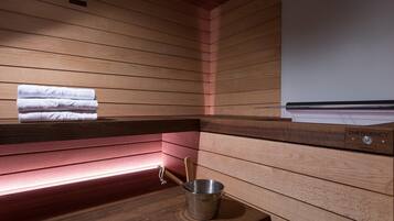 Uma sauna com paredes de madeira, um banco, um porta-toalhas e um balde de metal com cabo de madeira.