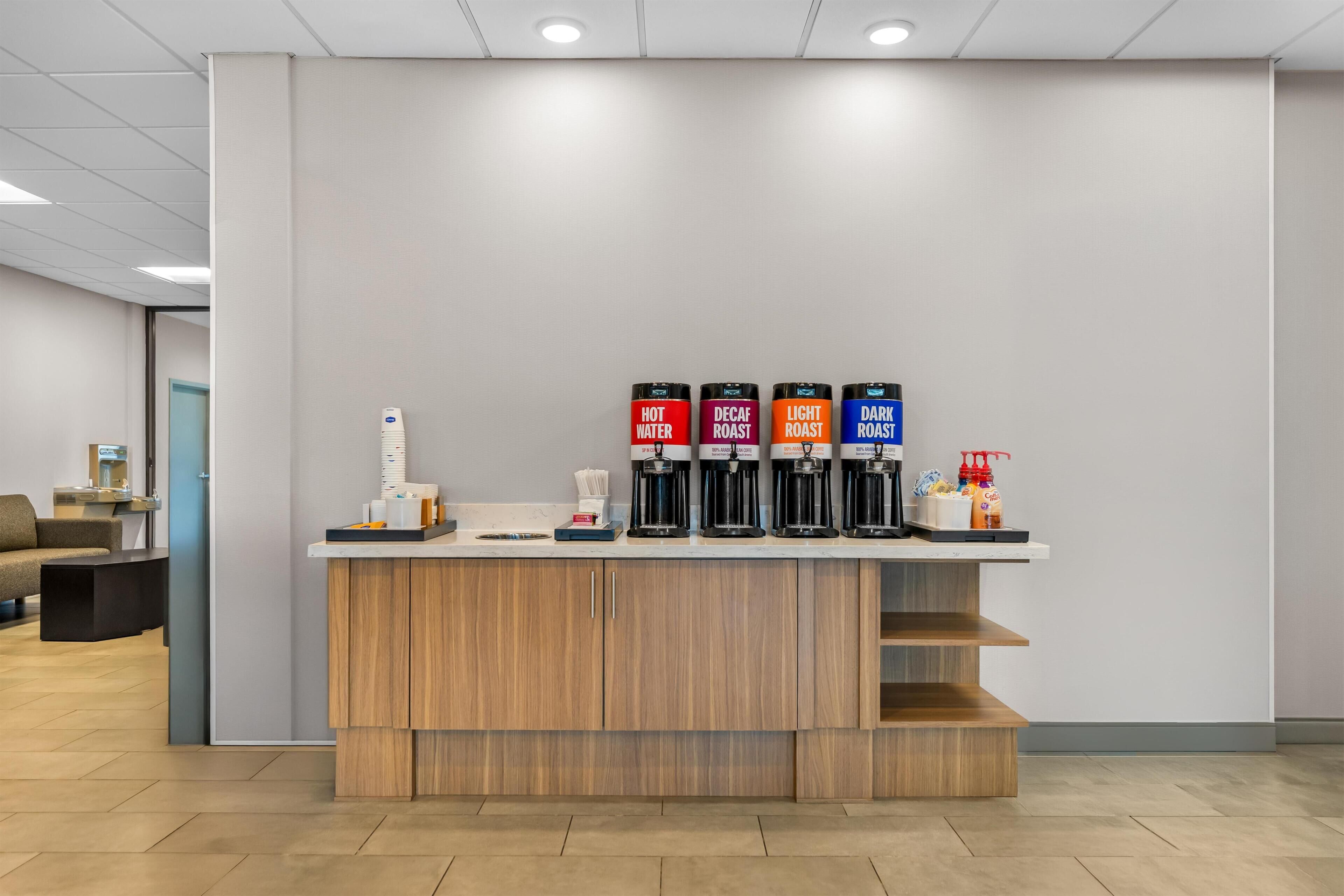 Uma área de recepção com estação de café, oferecendo água quente, café descafeinado, torra clara e torra escura.