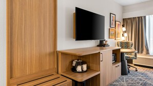 Quarto de hotel com uma mesa de madeira, televisão de tela plana, sofá e uma janela grande com cortinas.