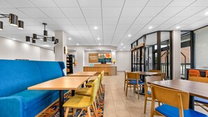 Um lobby moderno de hotel com um sofá azul, mesas e cadeiras de madeira, um balcão de recepção e um tapete estampado.