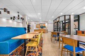 Um lobby moderno de hotel com um sofá azul, mesas e cadeiras de madeira, um balcão de recepção e um tapete estampado.