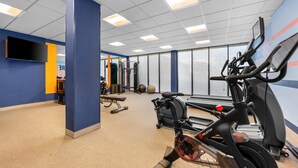 Academia com equipamentos de ginástica, televisão e uma janela grande.