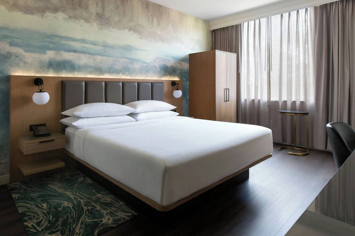 Quarto de hotel moderno com uma cama grande, uma mesa de cabeceira, uma escrivaninha e um guarda-roupa.