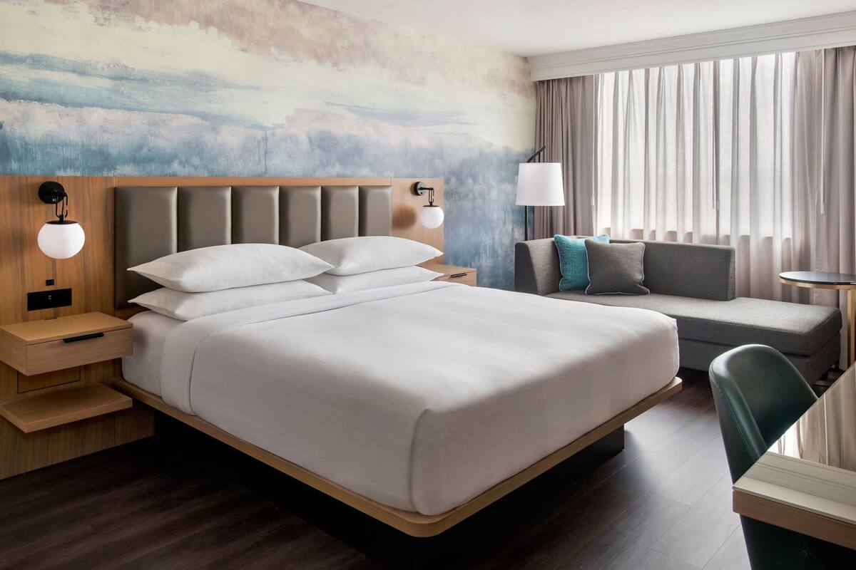 Quarto de hotel com uma cama grande, um sofá, uma escrivaninha e uma luminária.