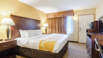 Quarto de hotel com uma cama grande, duas mesas de cabeceira com luminárias, um aparador com espelho e uma televisão.
