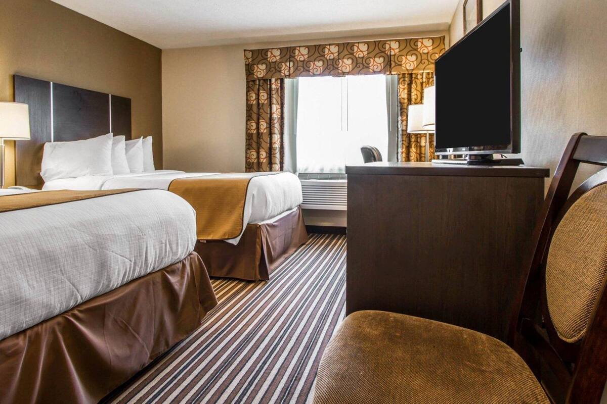 Quarto de hotel com duas camas, televisão, escrivaninha e uma cadeira.