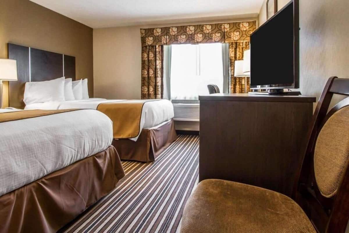 Quarto de hotel com duas camas, uma escrivaninha, televisão e uma janela com cortinas.