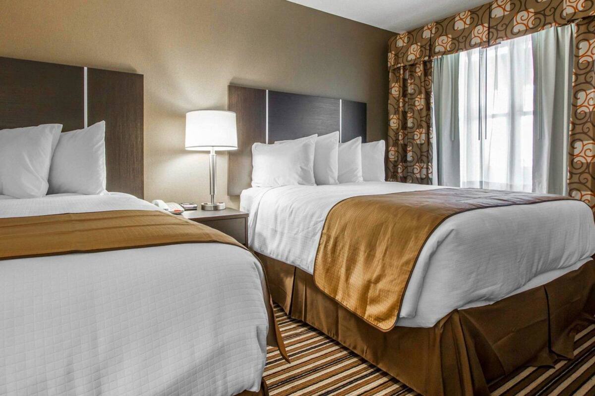 Quarto de hotel com duas camas, uma mesa de cabeceira com abajur e uma janela com cortinas.
