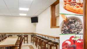 Uma sala de conferências com uma mesa comprida e várias cadeiras, uma TV de tela plana fixada na parede e um cartaz com imagens de waffles, chocolate e maçãs.