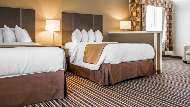Quarto de hotel com duas camas, uma escrivaninha e uma janela grande com cortinas.