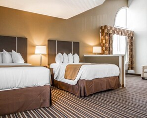 Quarto de hotel com duas camas, uma escrivaninha e uma janela grande com cortinas.