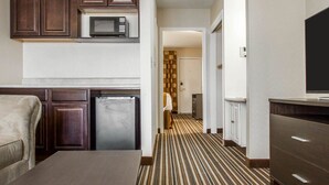 Quarto de hotel com cozinha compacta, televisão de tela plana, carpete listrado e vista para o corredor.