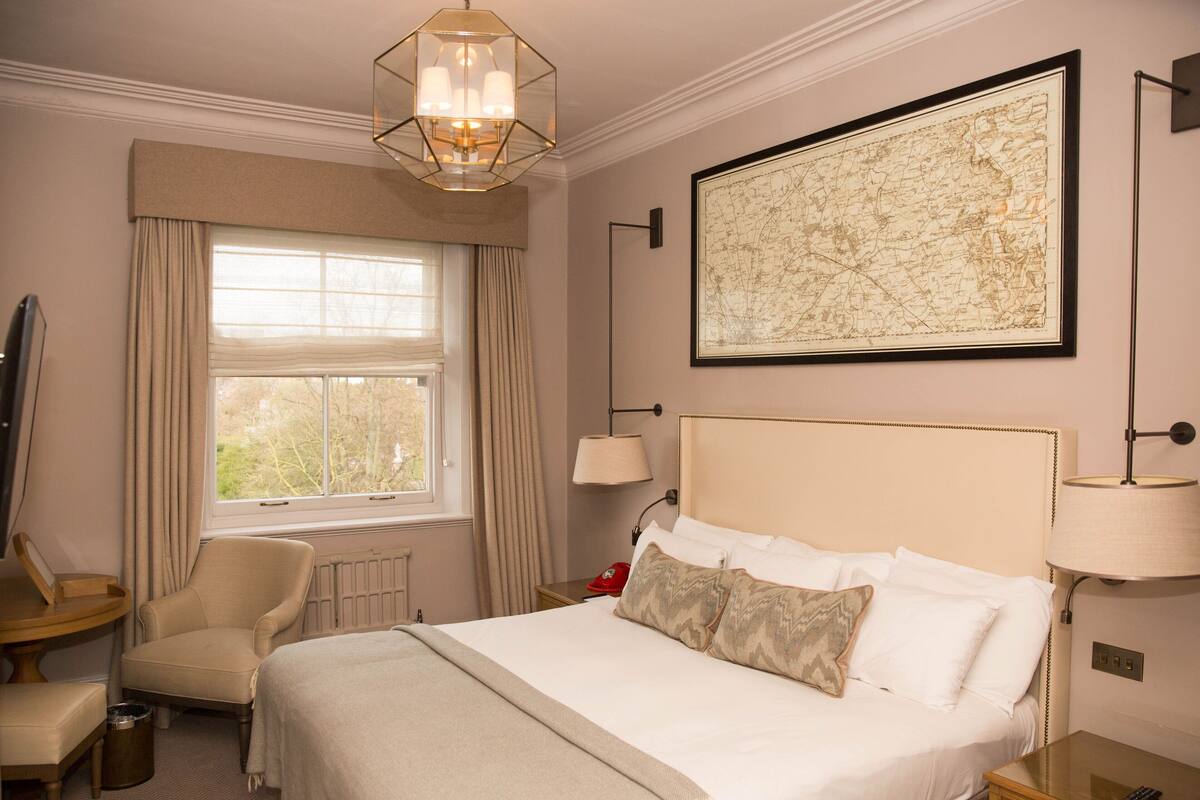 Quarto de hotel com uma cama grande, um mapa na parede, uma cadeira, um abajur e uma janela com cortinas.