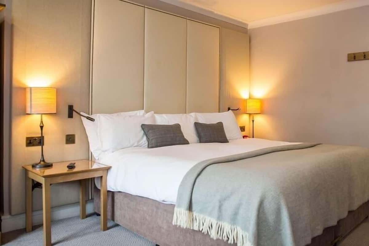 Quarto com cama, luminárias de cabeceira, mesa de cabeceira e uma porta.