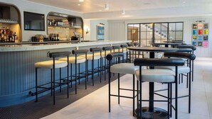 Uma área de bar com banquetas altas e balcão, uma escada e uma parede com quadros emoldurados.