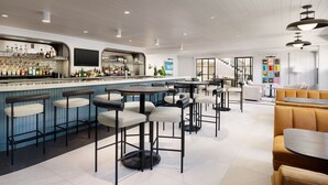 Uma área de bar moderna com bancos altos, um balcão com garrafas e um espaço de estar com mesas e cadeiras.