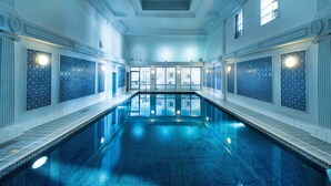 Uma grande piscina interna com paredes revestidas e uma clarabóia.
