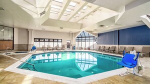 Uma piscina interior com água azul cristalina, chão em mosaico e teto com claraboias.