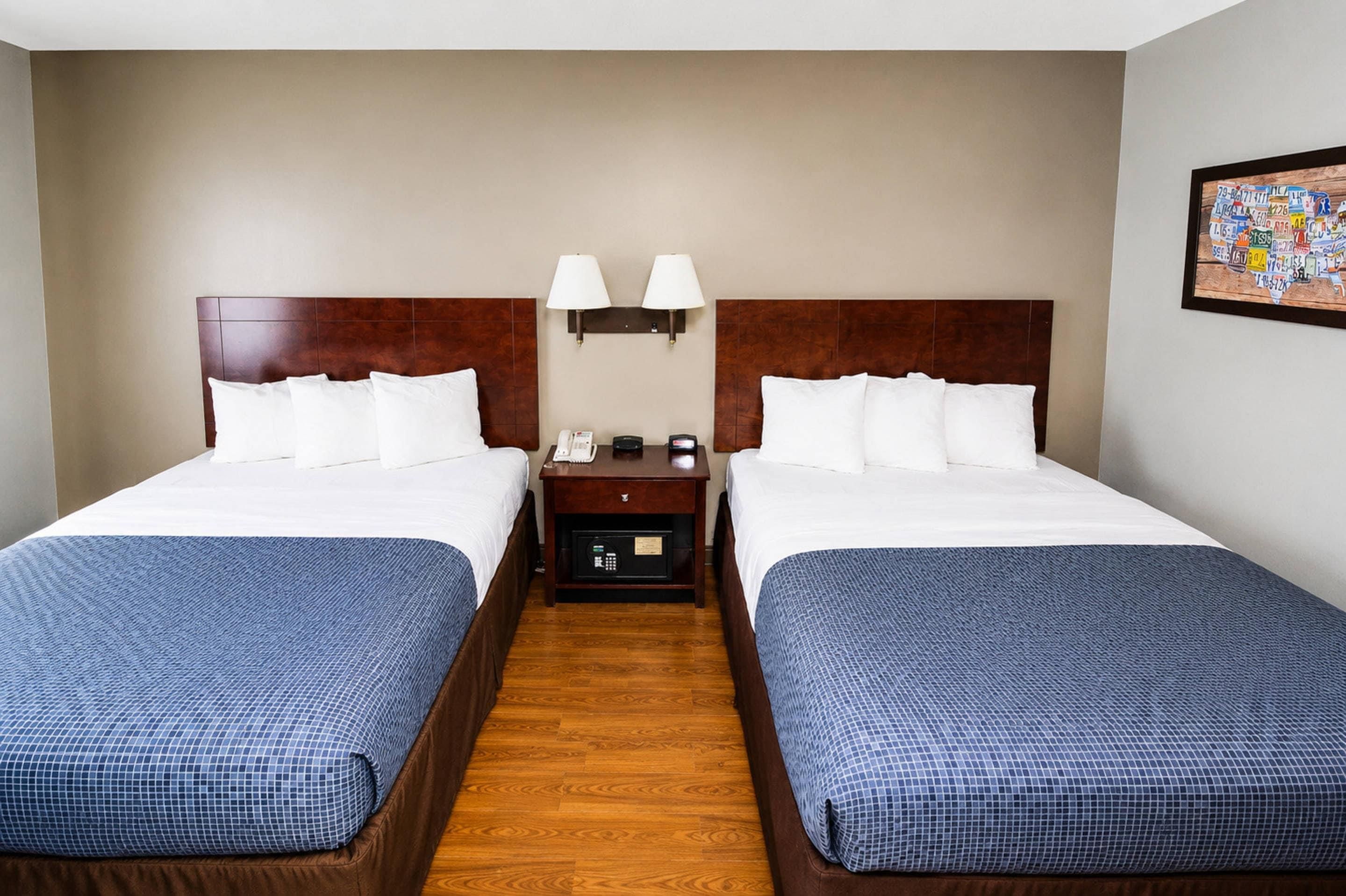 Quarto de hotel com duas camas, mesa de cabeceira com telefone e luminária, e obra de arte pendurada na parede.